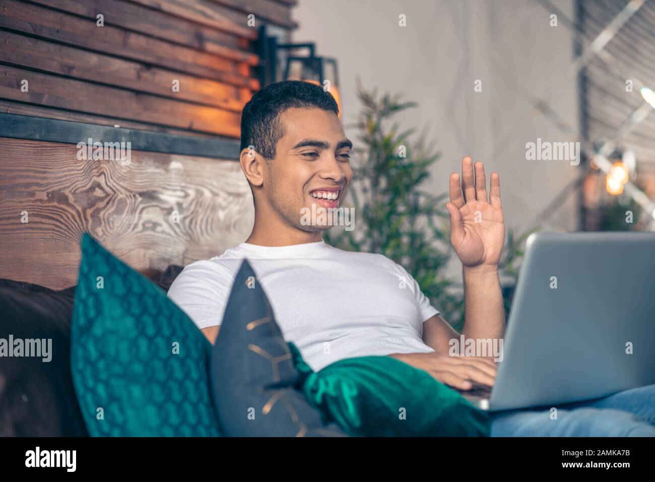Guy raising his hand while smiling and greeting Stock Photo - Alamy