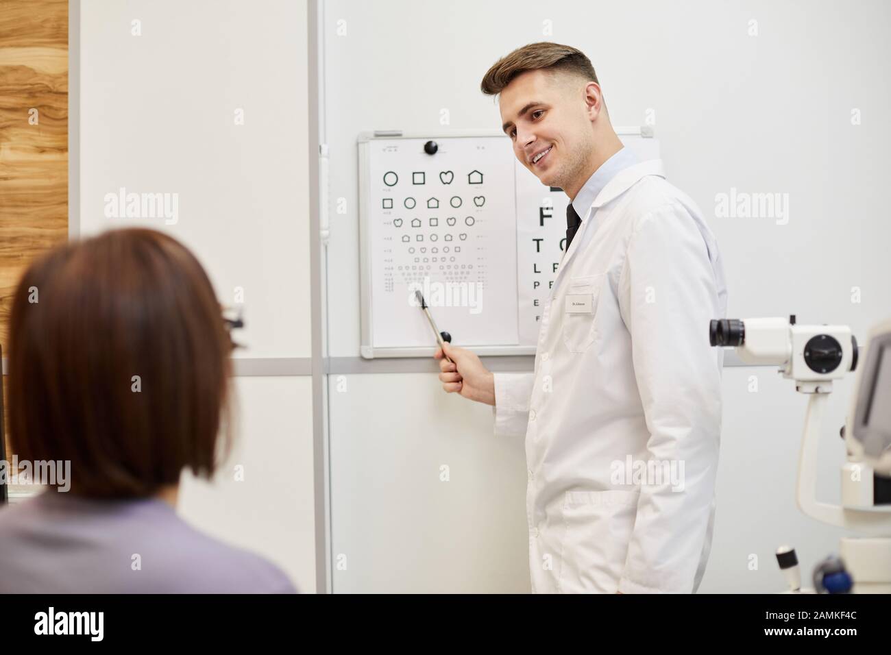 Portrait of smiling young optometrist pointing at vision chart while ...