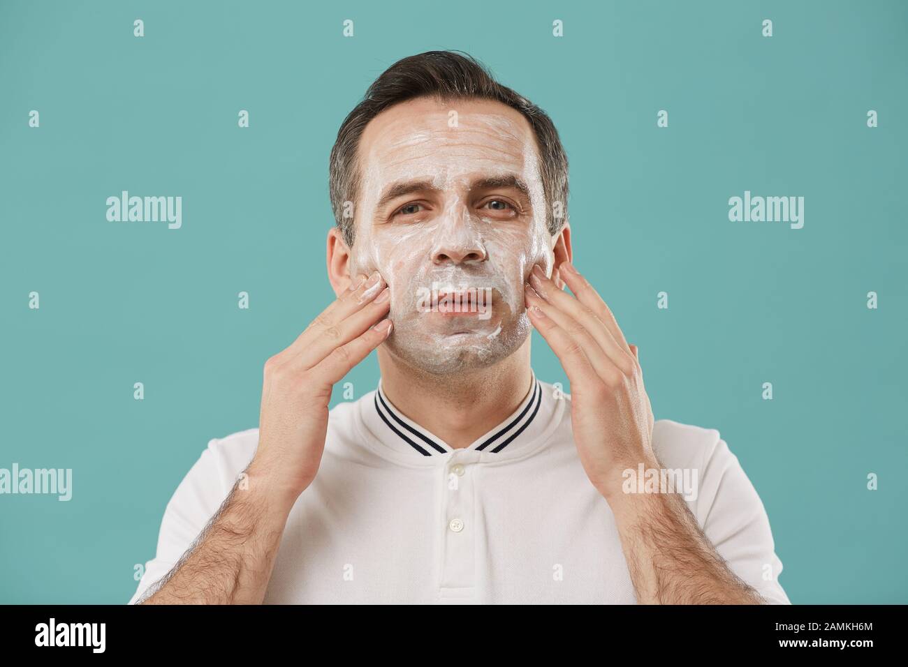 Head and shoulders portrait of handsome adult man applying face cream ...