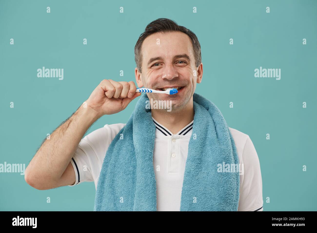 Waist up portrait of smiling middle aged man brushing teeth while ...