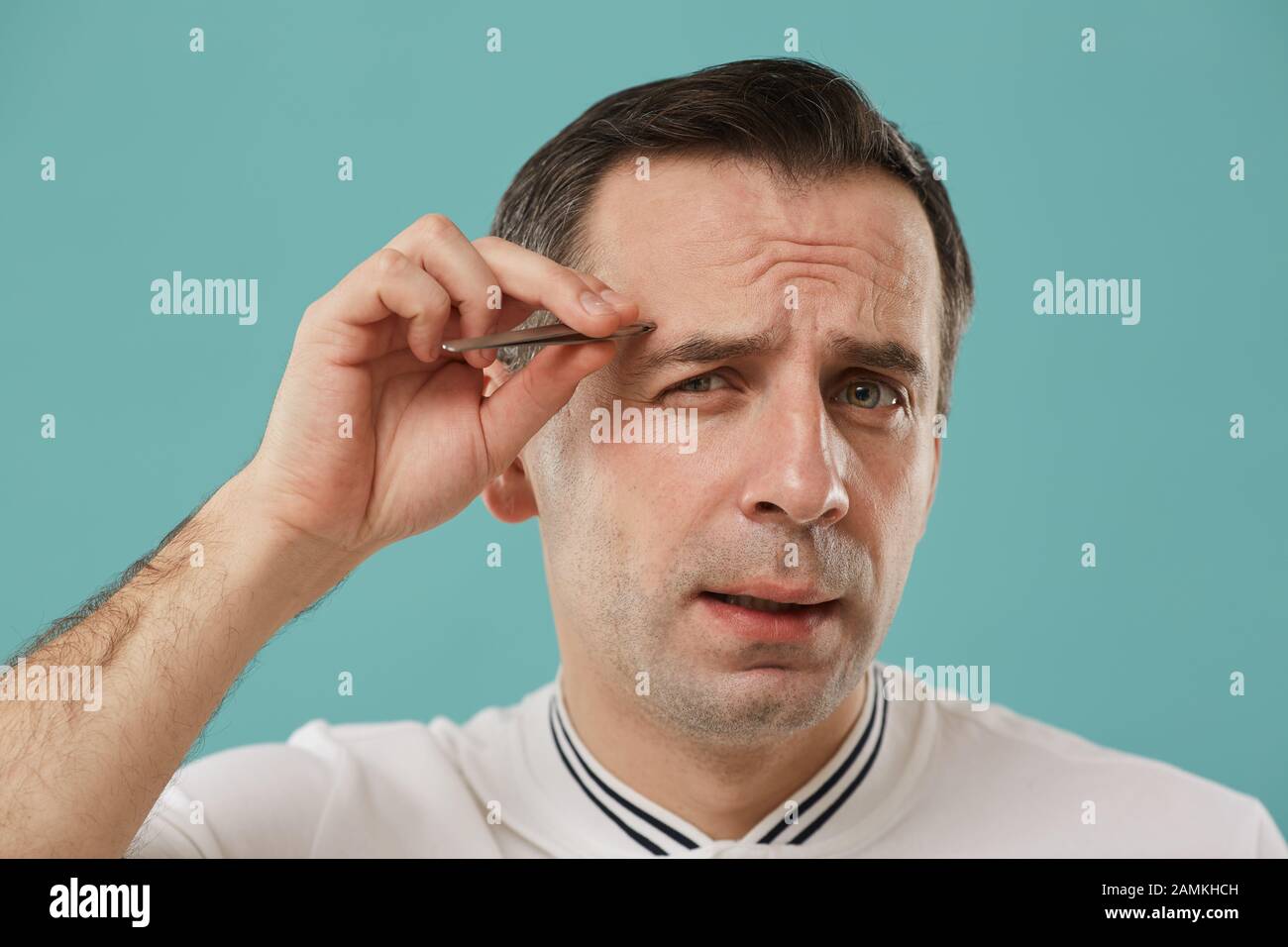 Head and shoulders portrait of wincing middle aged man plucking ...
