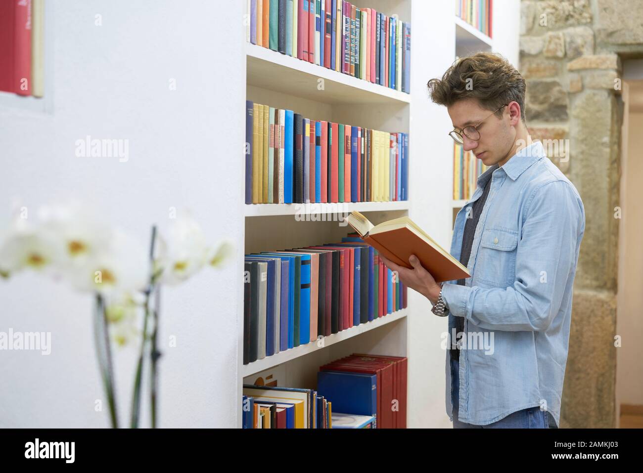 Handsome young student with glasses lost in reading a book in home ...