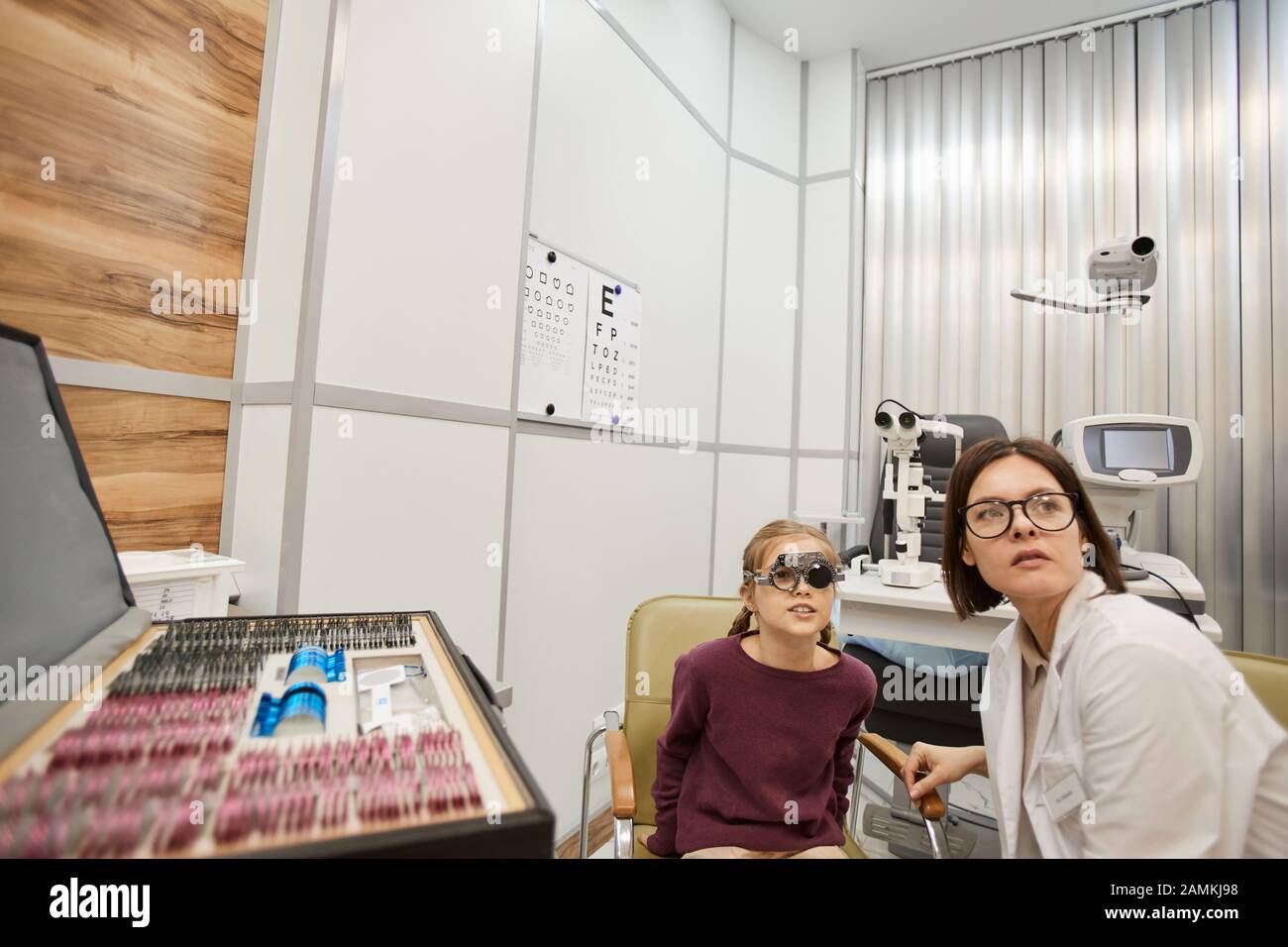 Wide angle view at of female optometrist checking eyesight of little ...