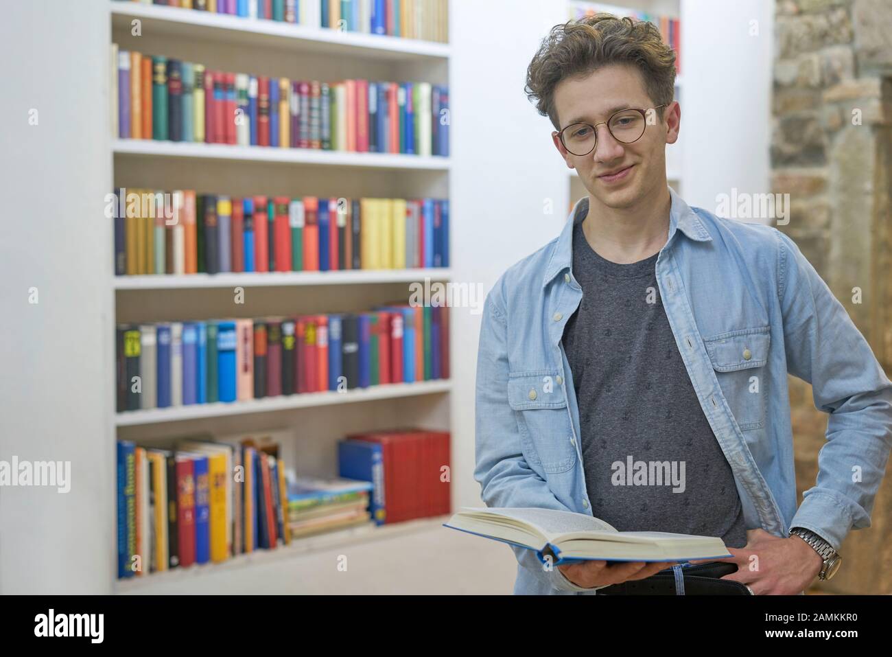 Young handsome man in library is smiling because of the book he is ...