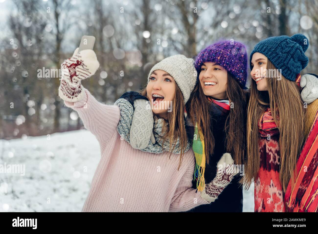 Three women friends outdoors in knitted hats using mobile phone on a ...