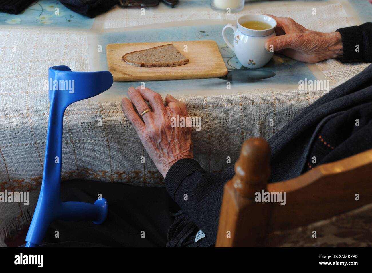An old man at the kitchen table, in front of him a slice of bread and a ...