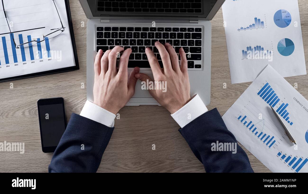 Male entering analyzed data of graphs on laptop computer at office, top ...