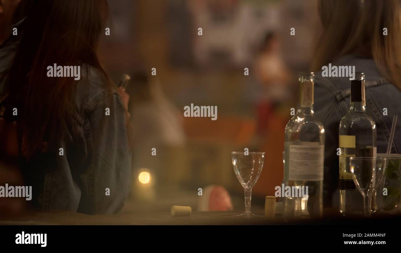 Wine and glasses on bar counter, two women drinking alcohol at club ...