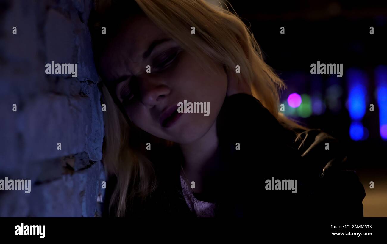 Beautiful blonde woman crying, leaning at wall, suffering after break ...