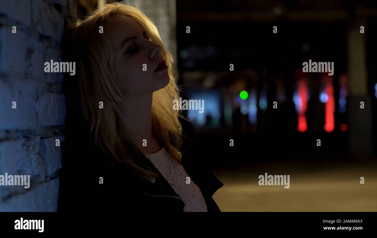 Sad blonde woman standing alone outside nightclub, melancholy ...