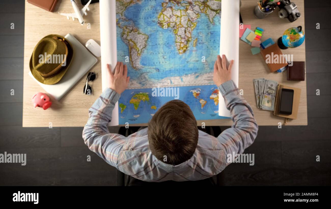 Male unfolding world map to choose country for travel destination ...