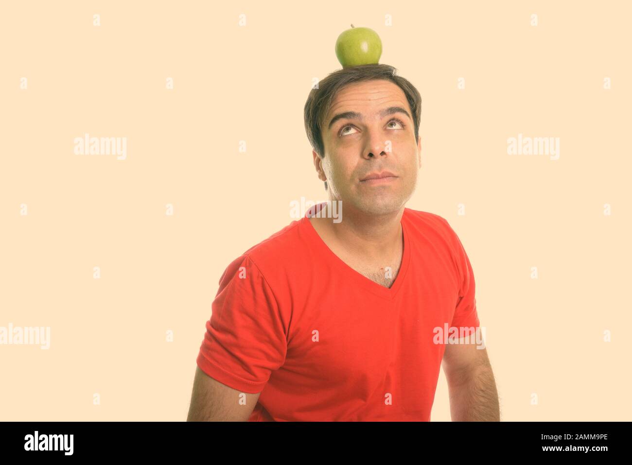 Studio shot of young Persian man thinking while looking at green apple ...