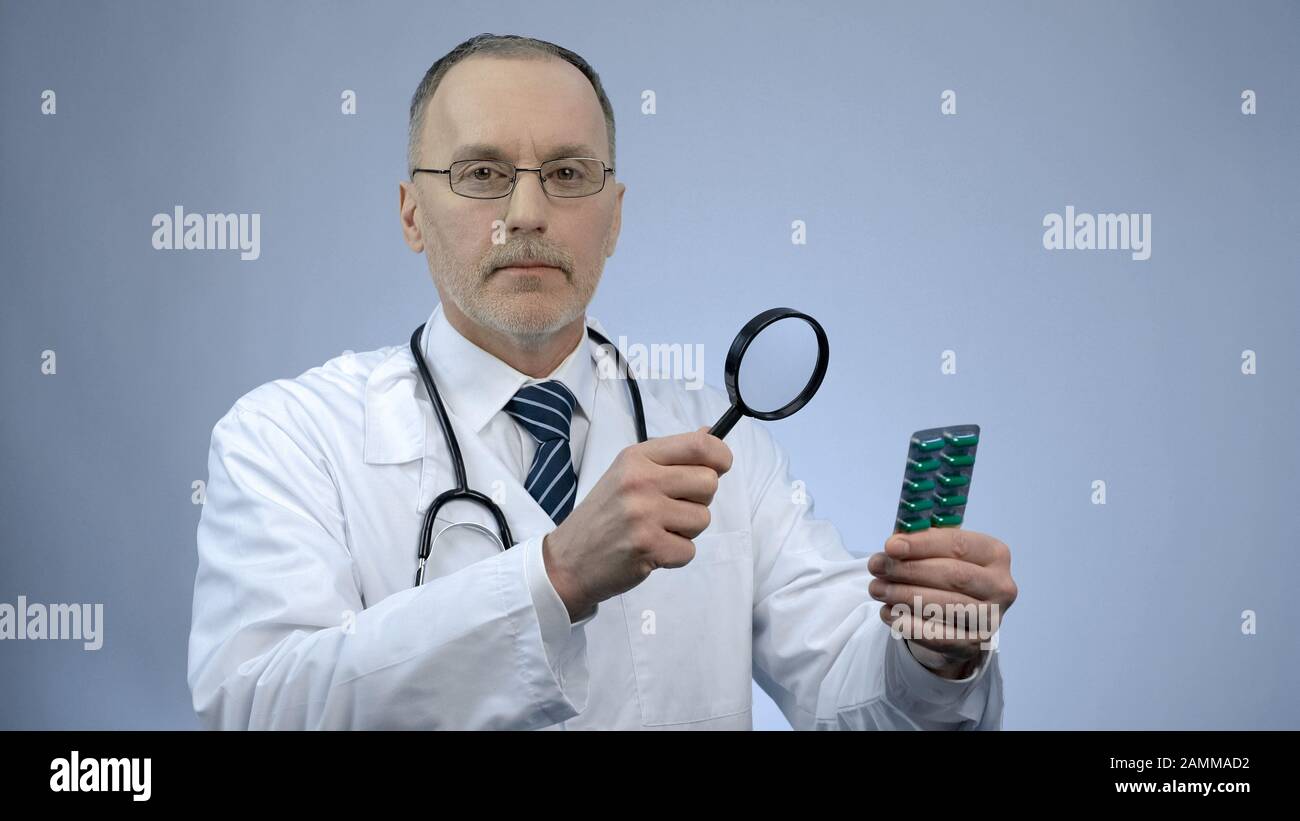 Doctor examining pack of pills with magnifying glass, counterfeit ...