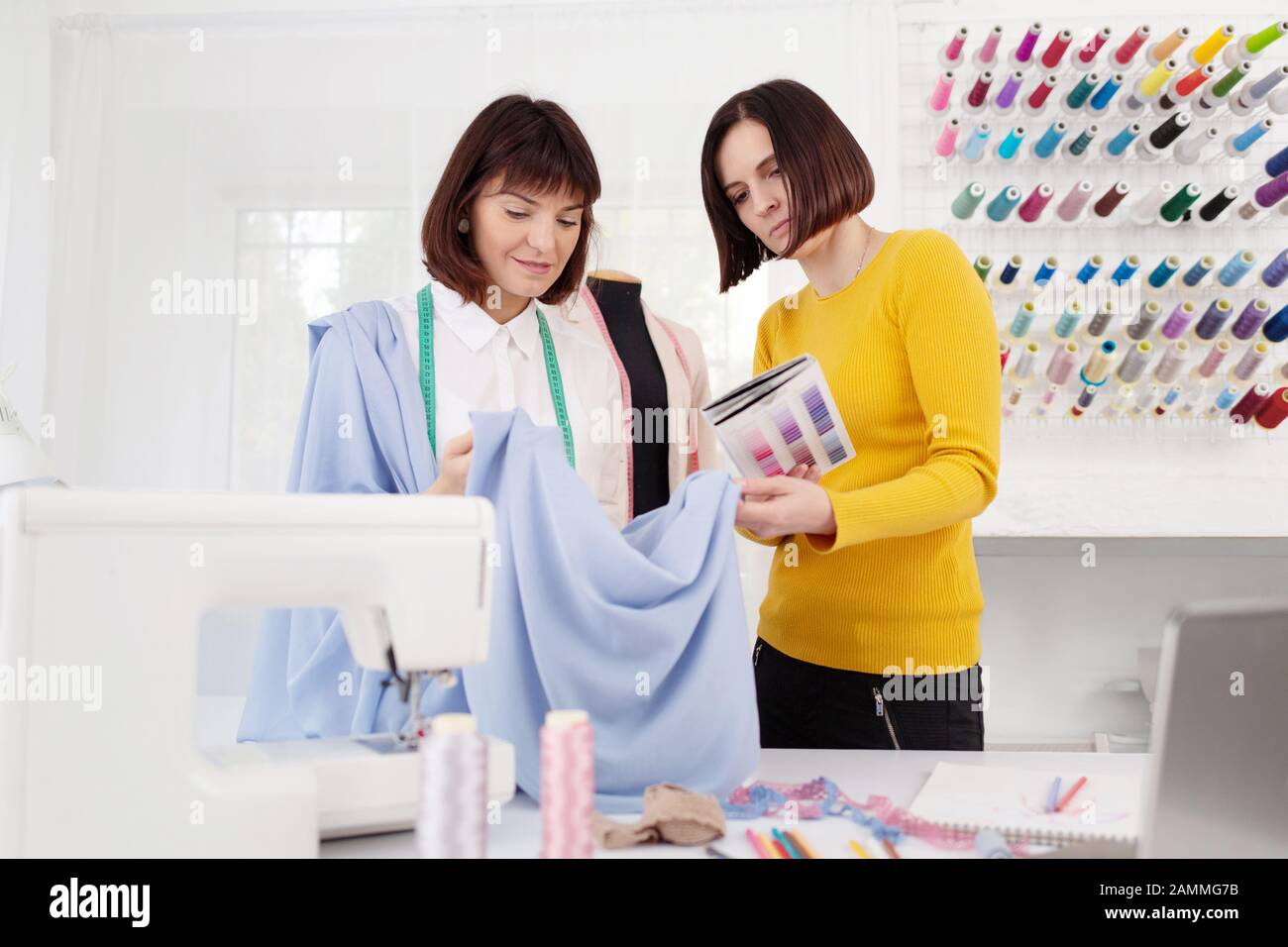 Two young female dressmakers working in sewing studio. Seamstress ...