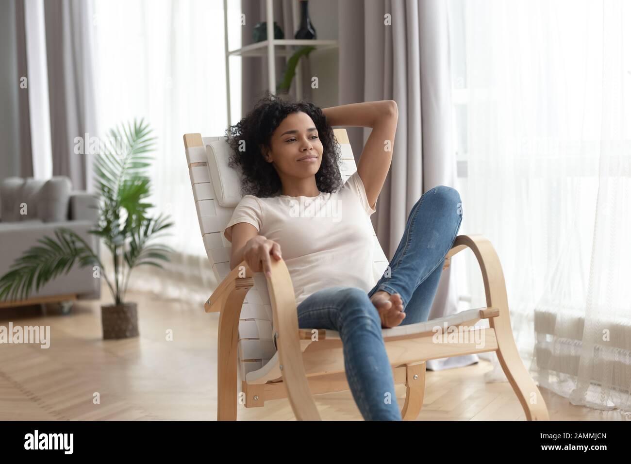 Attractive african woman leaned on wooden rocking chair resting indoors ...