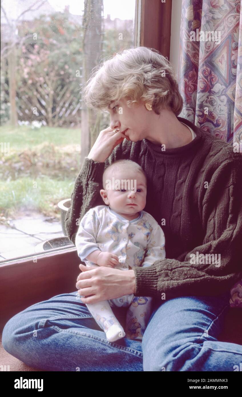 young mother suffering from post natal depression with her baby sitting ...