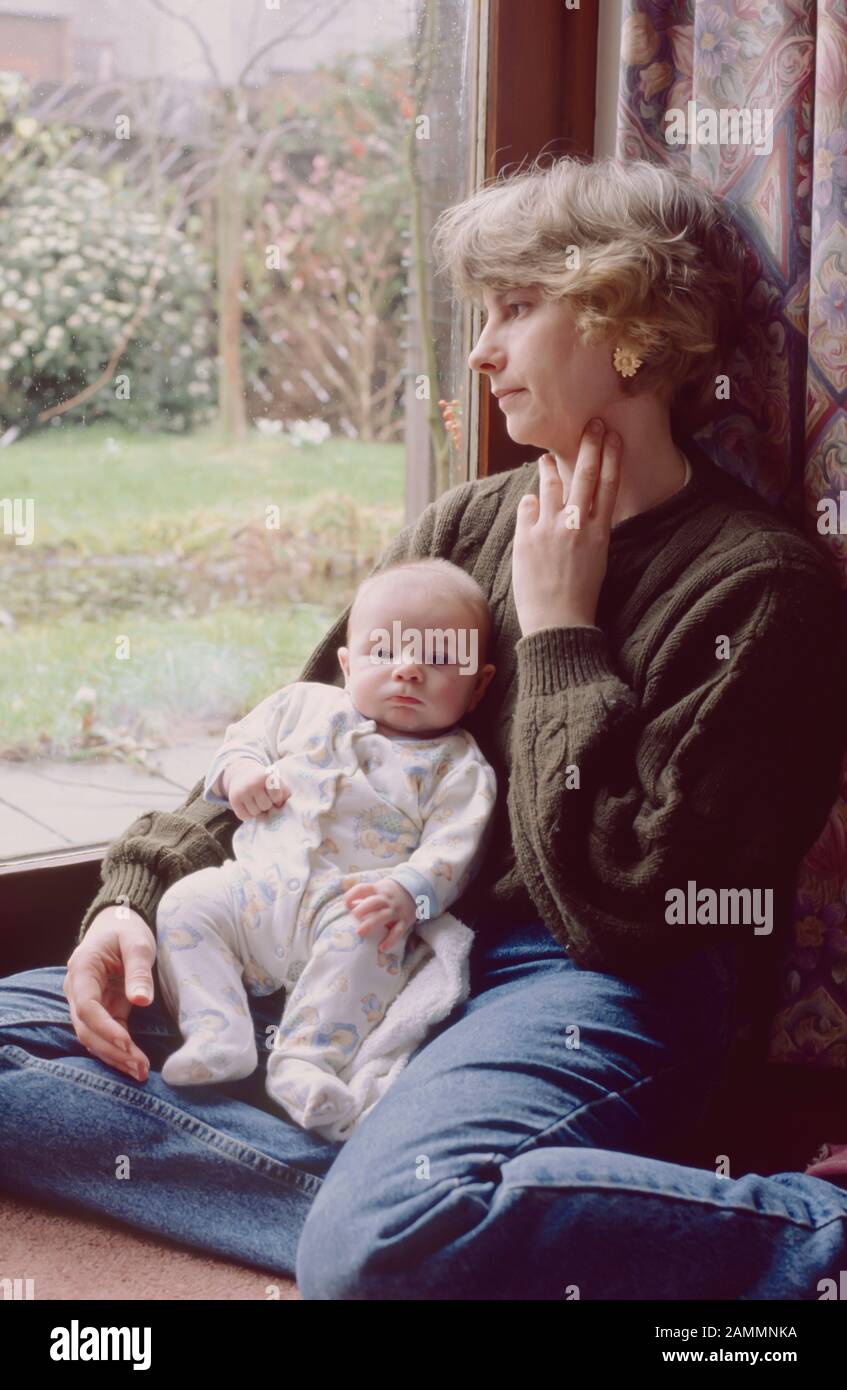 young mother suffering from post natal depression with her baby sitting ...
