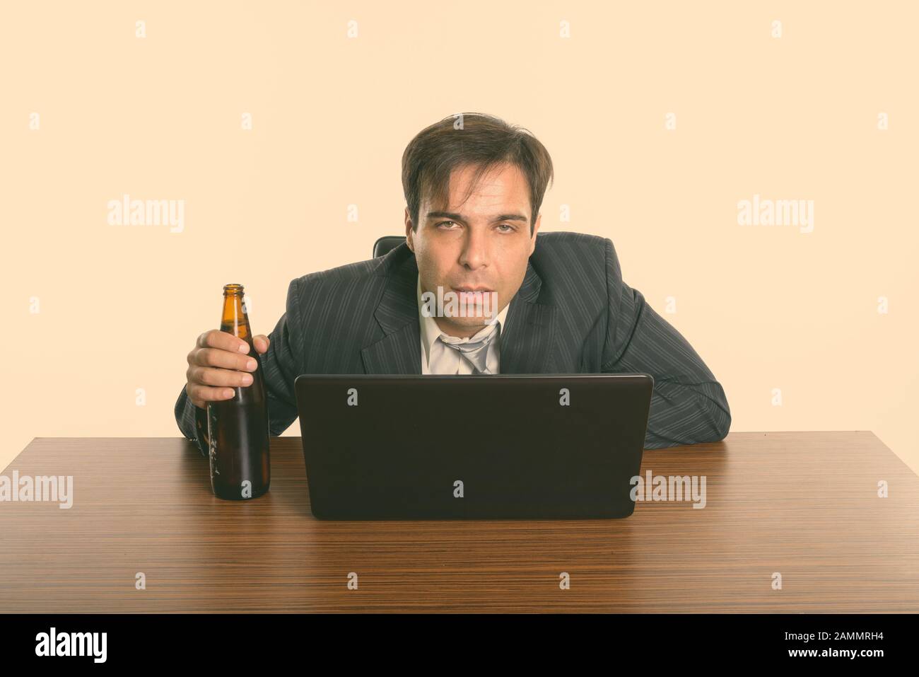 Persian businessman looking drunk while holding bottle of beer at work ...