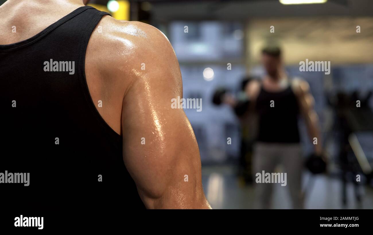 Sweaty sportsman pumping arm muscles, holding dumbbells in hands close ...