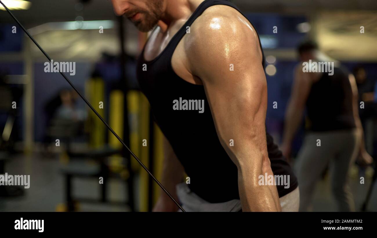 Guy working hard in gym doing brisk pull-downs with one arm, finishing ...
