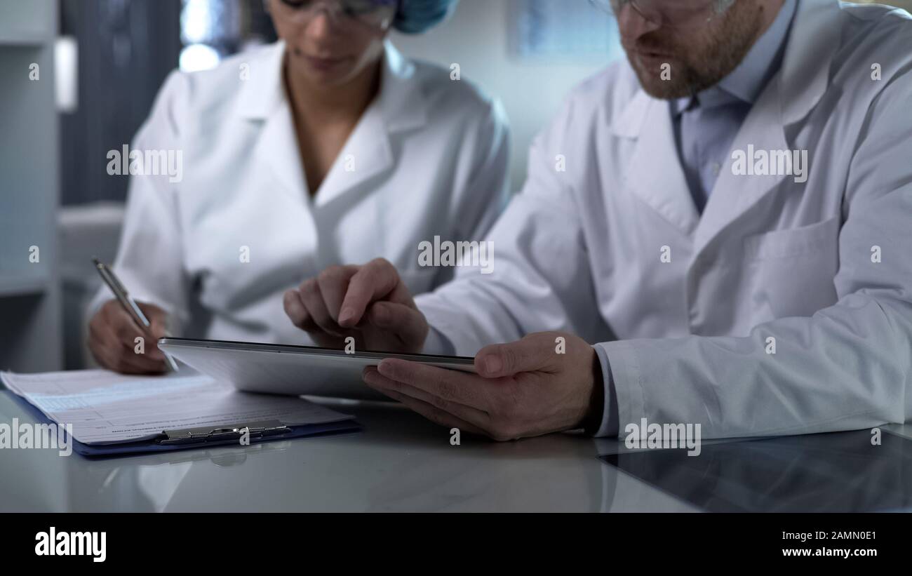 Scientist working on tablet and female assistant making notes, clinic ...