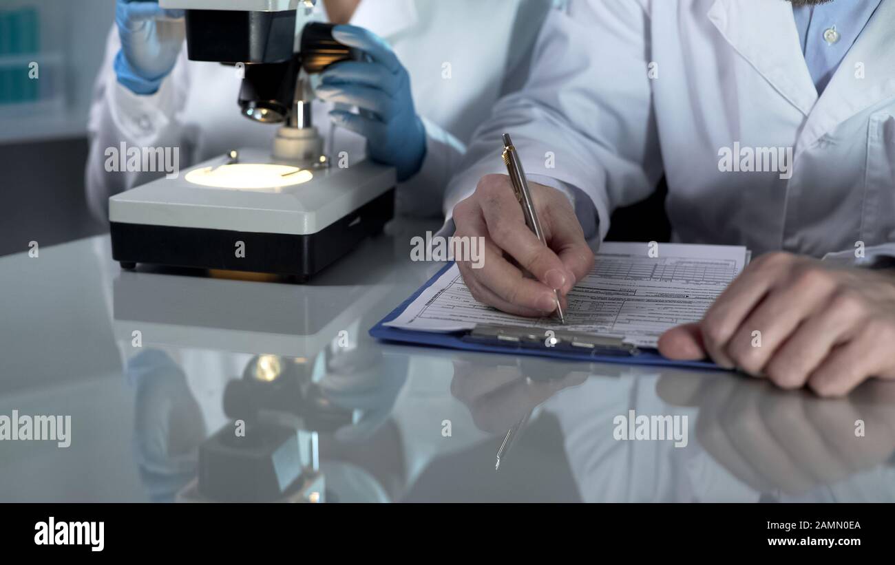 Lab worker filling paper forms, his assistant viewing samples under ...