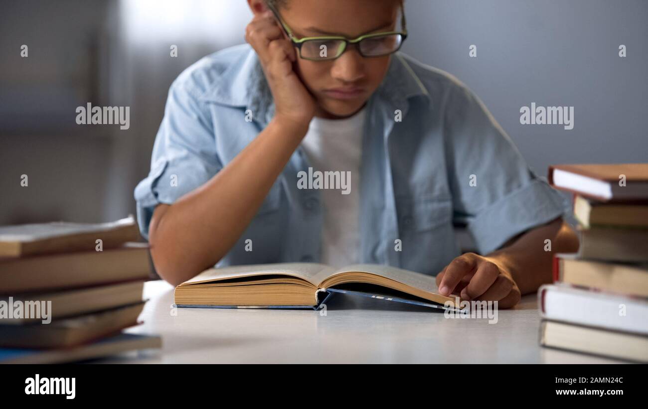 Smart little boy reading pile of books, preparing for exams ...