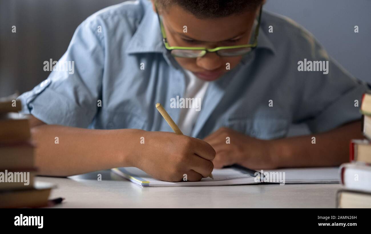 Elementary school pupil diligently writing letters in his notebook ...