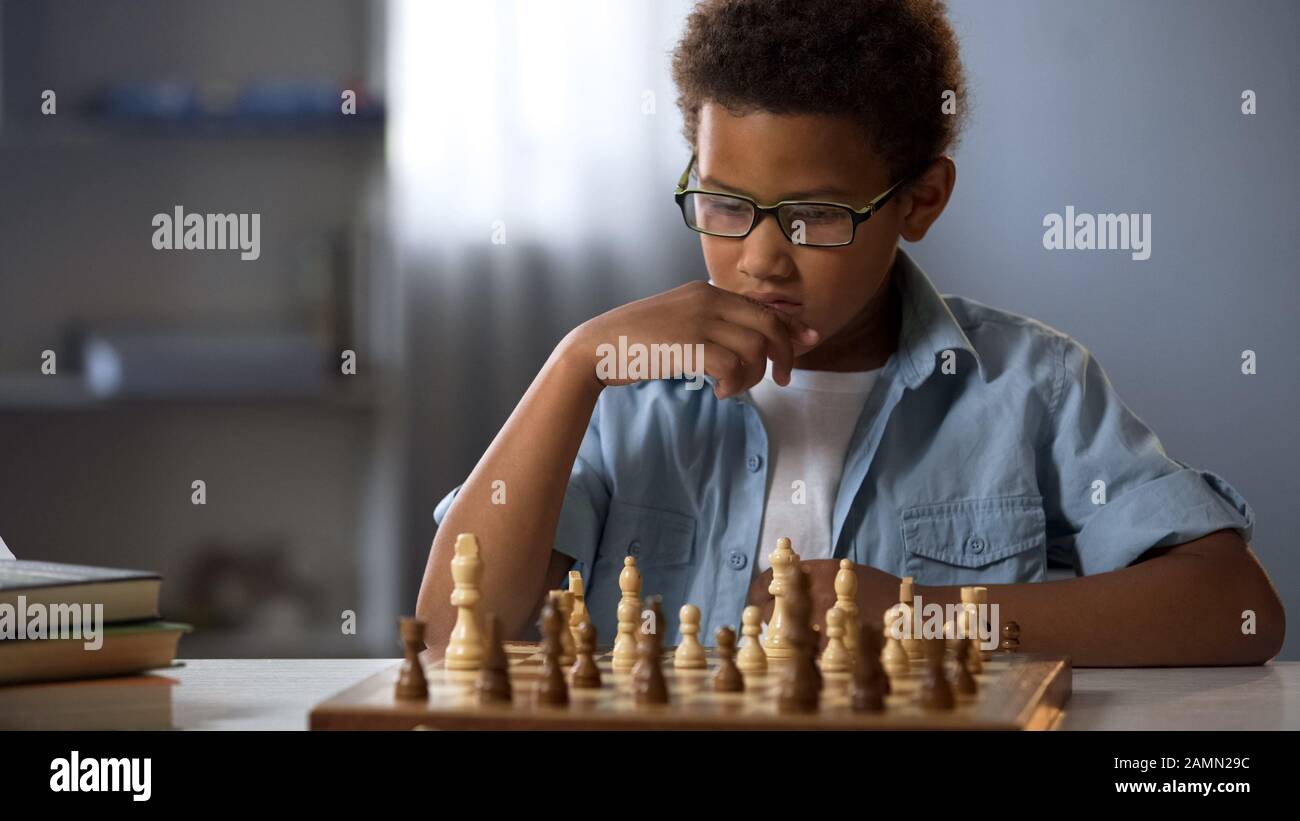 African American boy logically thinking out strategy of playing chess ...