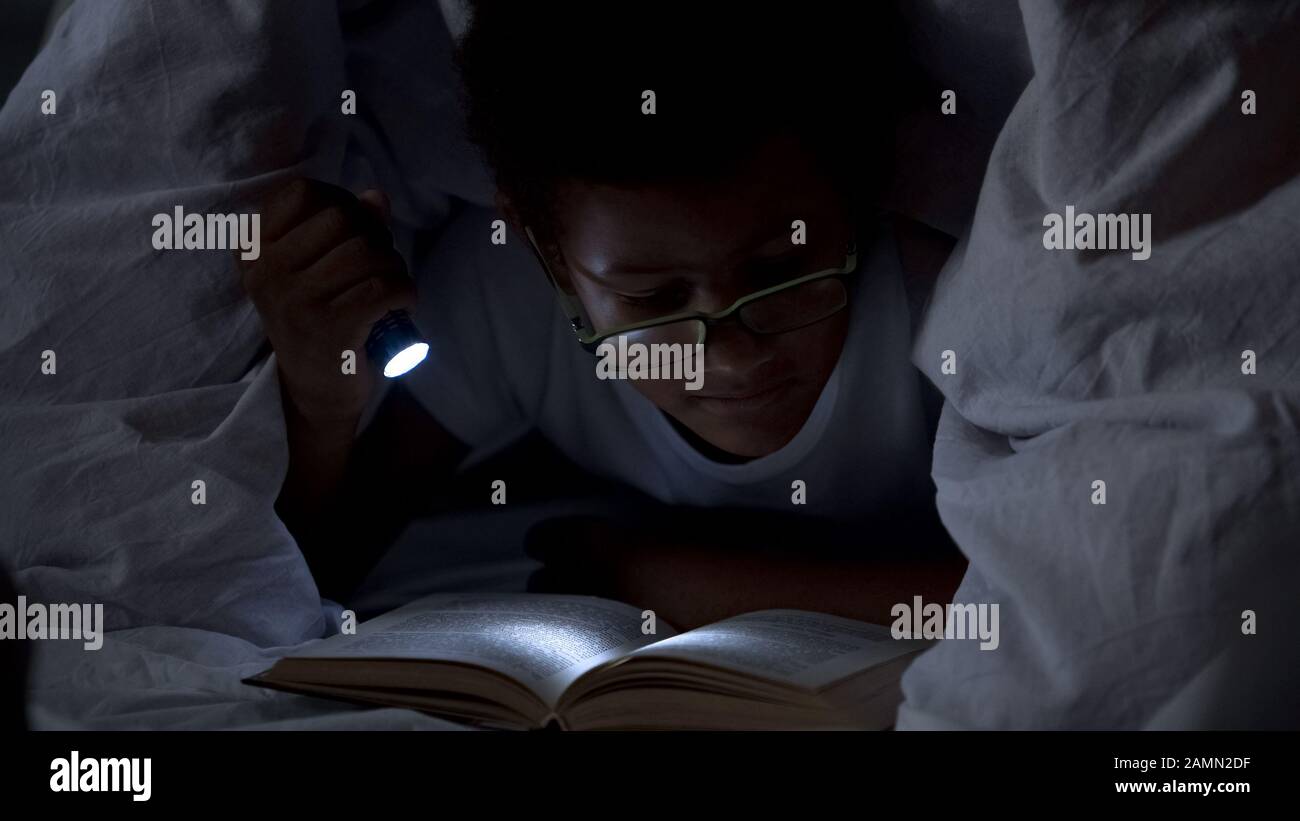 Child reading books at night under blanket, lighting himself with ...