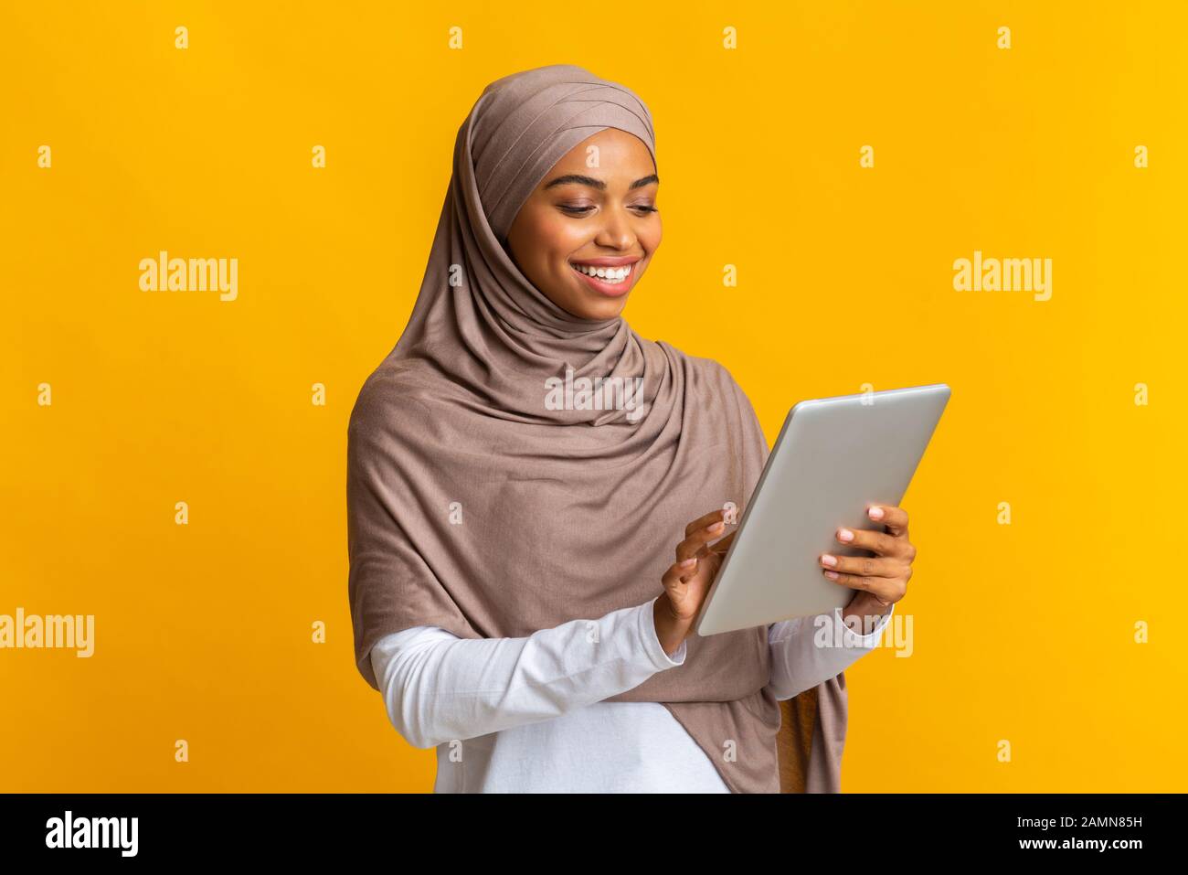 Portrait of smiling afro muslim girl in hijab using digital tablet ...