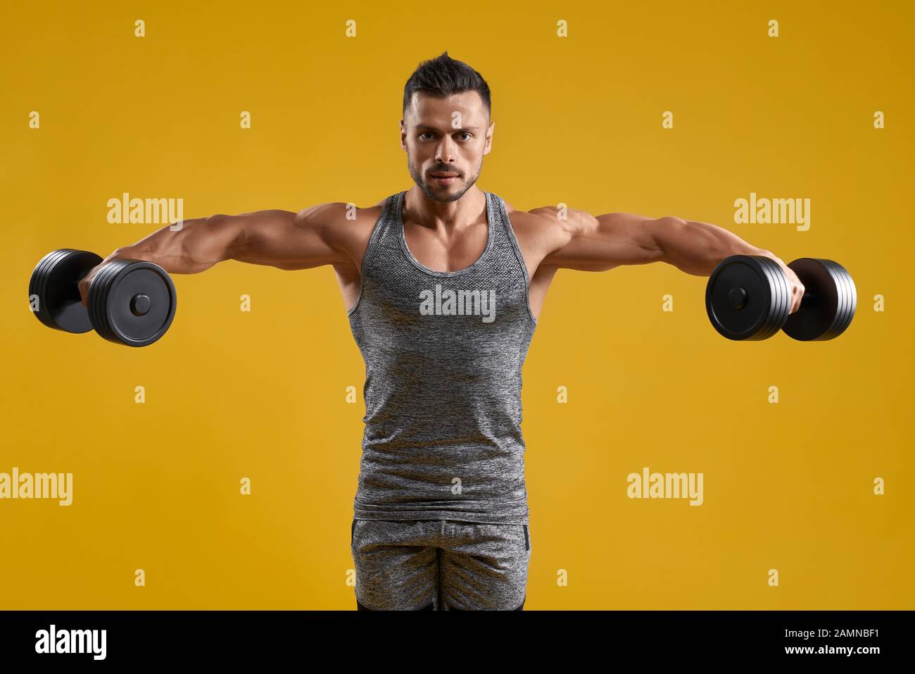 Front view of athletic gentleman in sport tank top lifting heavy ...