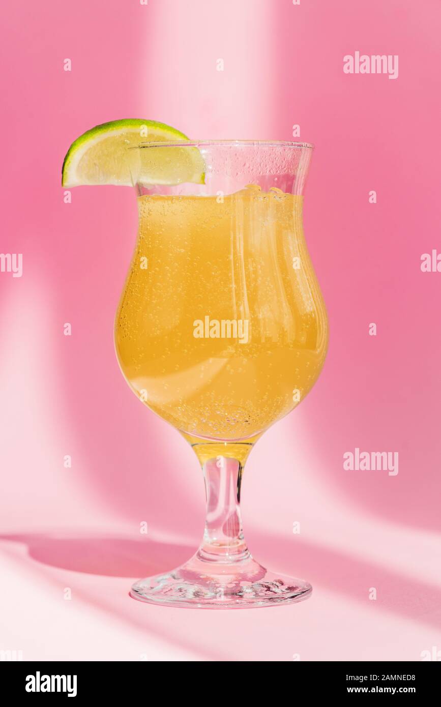 fresh yellow lemonade with lime slice in sunlight on pink background ...