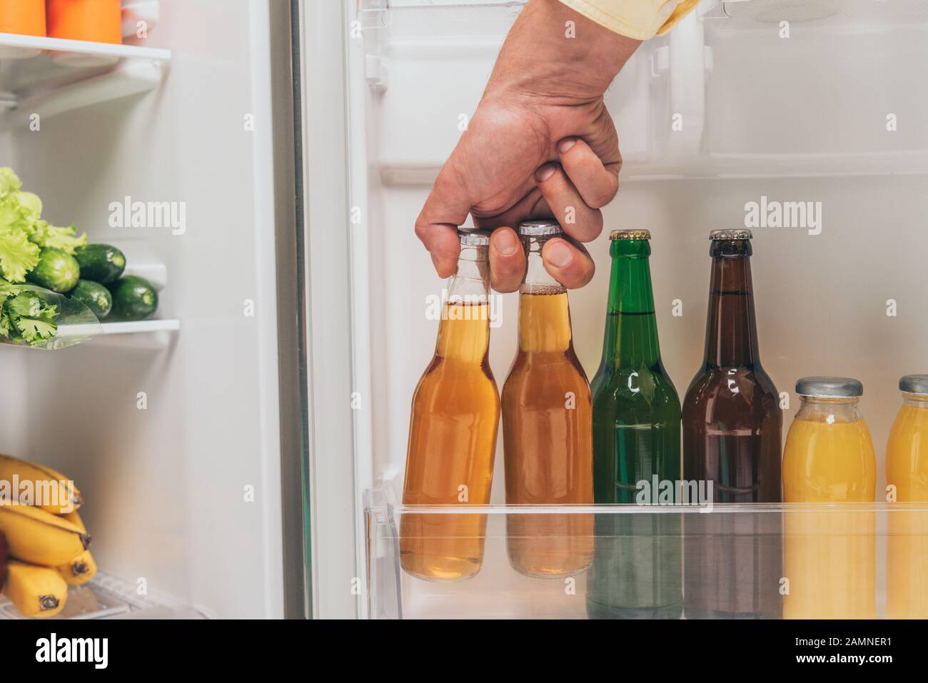 cropped view of man taking bottles of beer out from open fridge with ...