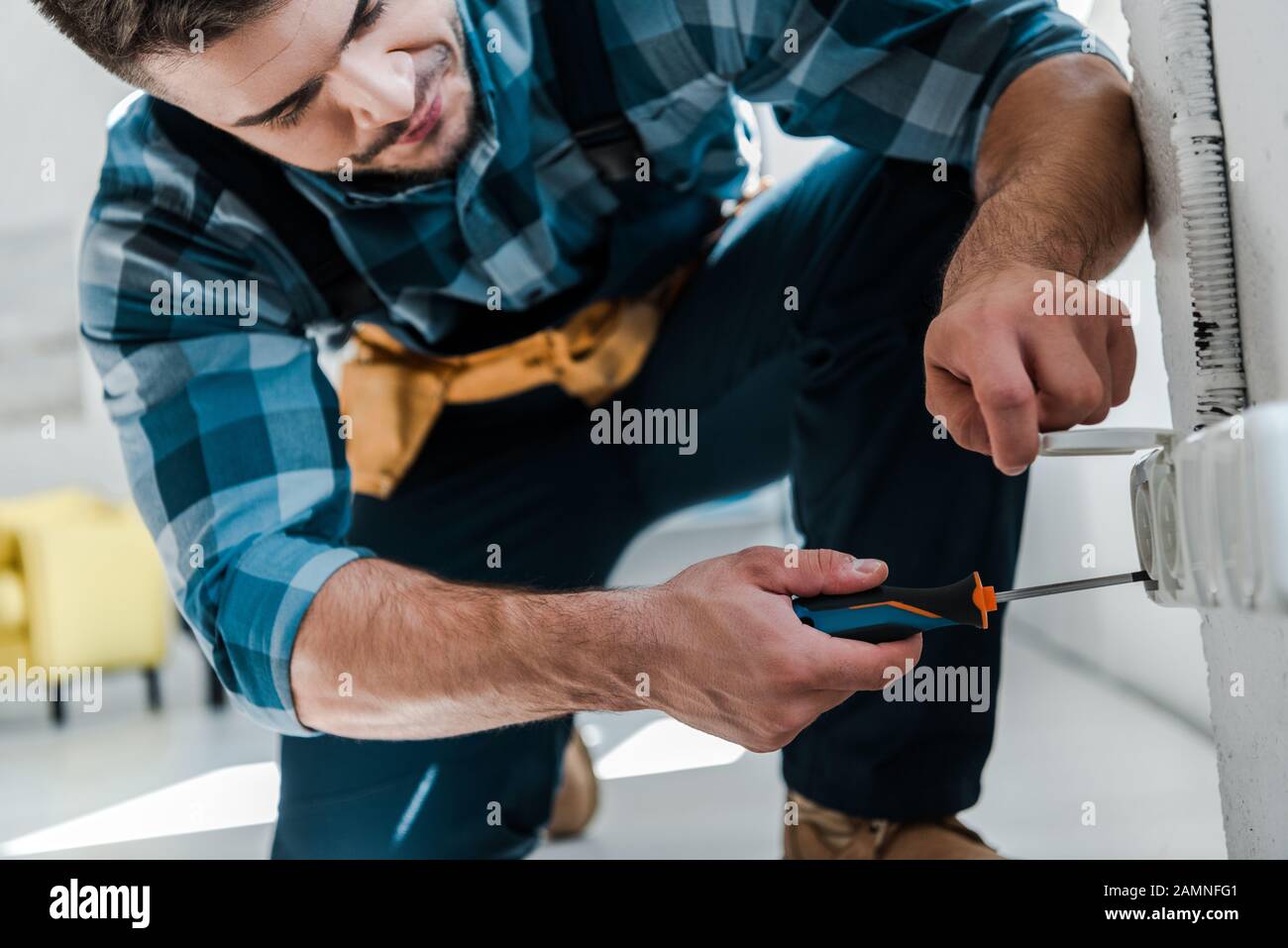 bearded repairman in uniform sitting while fixing power socket with ...