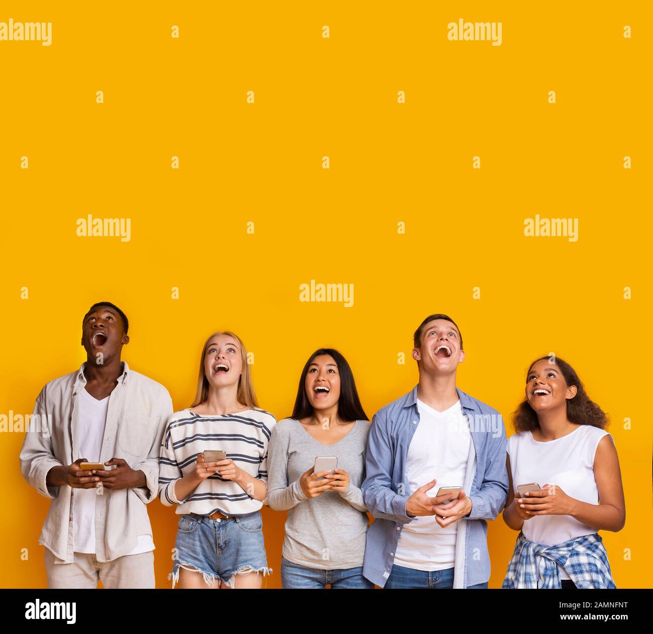 Group of surprised students with smartphones over yellow background ...