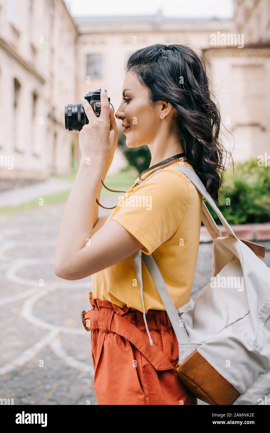 side view of beautiful girl holding digital camera while taking photo ...
