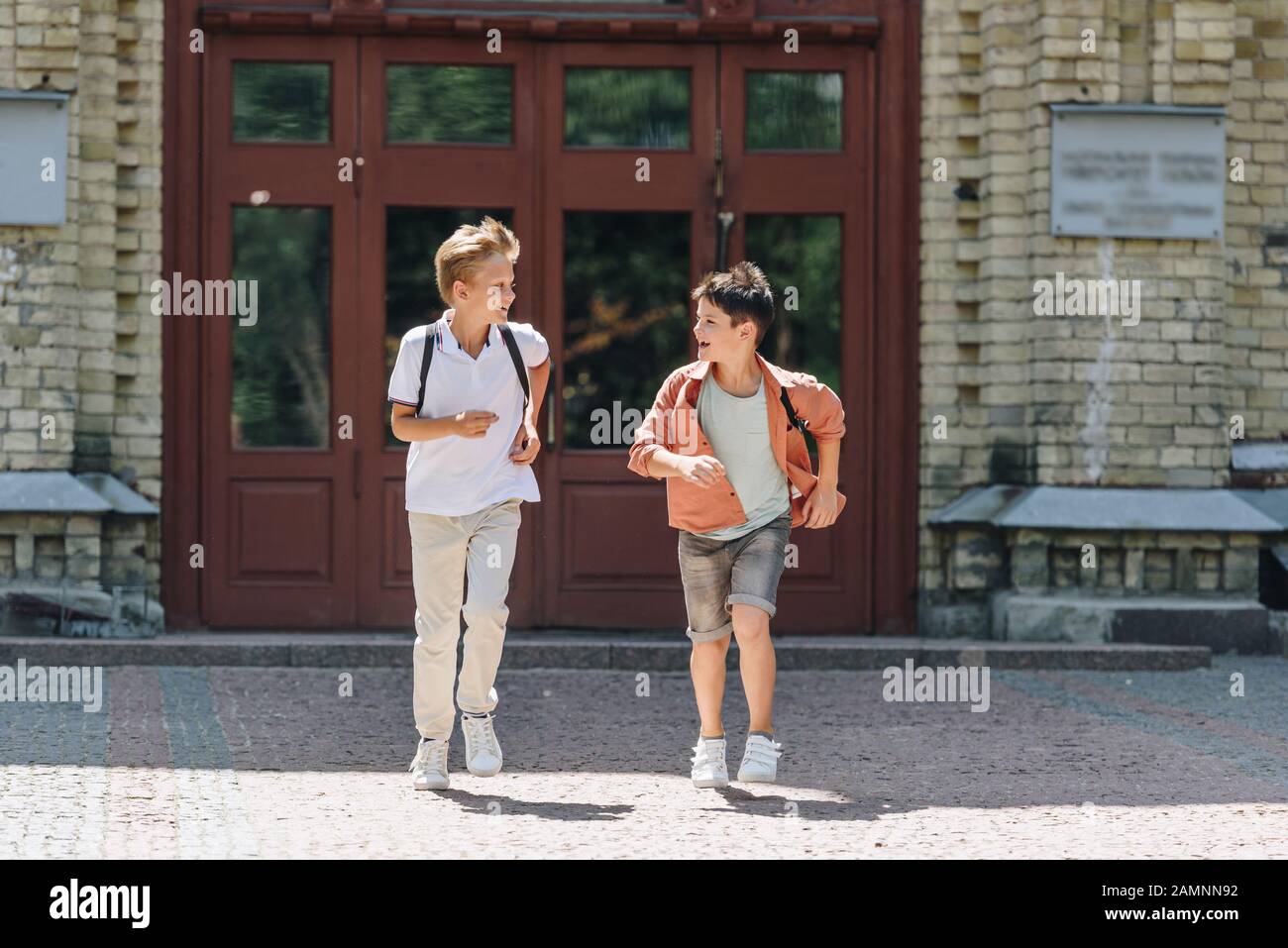 two cheerful schoolboys running in schoolyard while looking at each ...