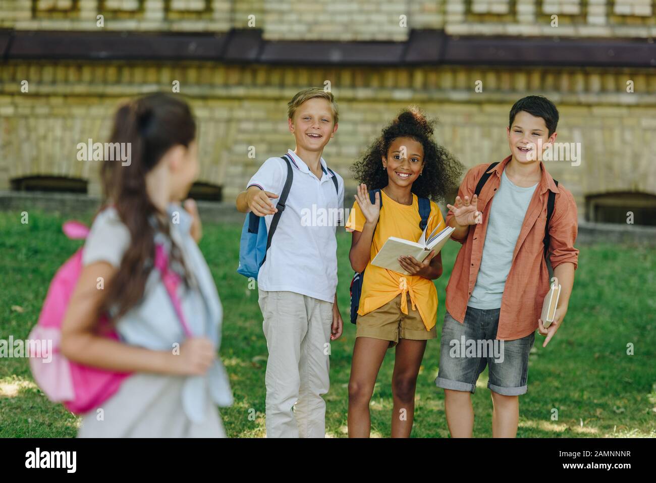 selective focus of multicultural schoolkids waving hands to schoolgirl ...