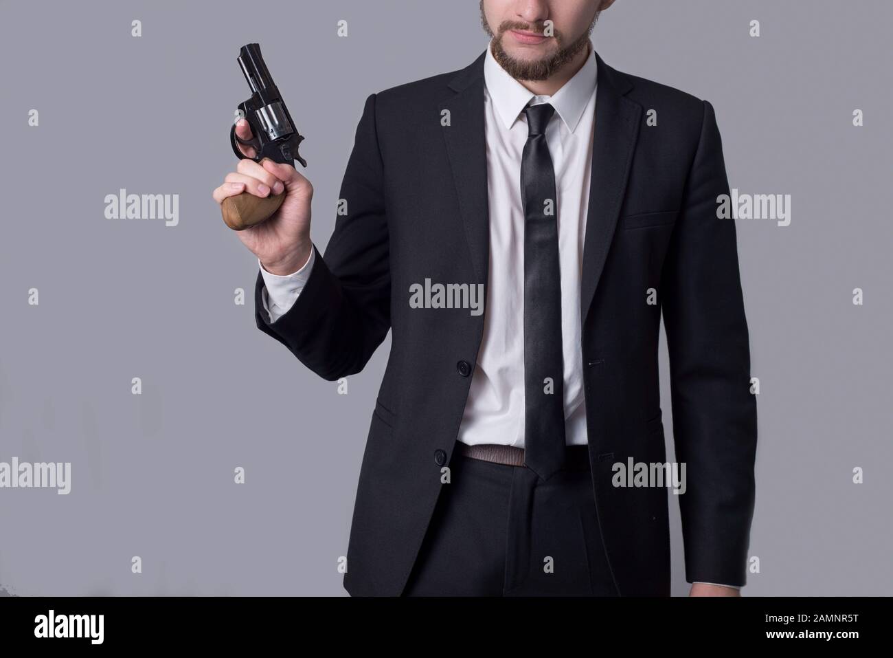 Portrait of a bearded man in a business suit holding a revolver. On a ...