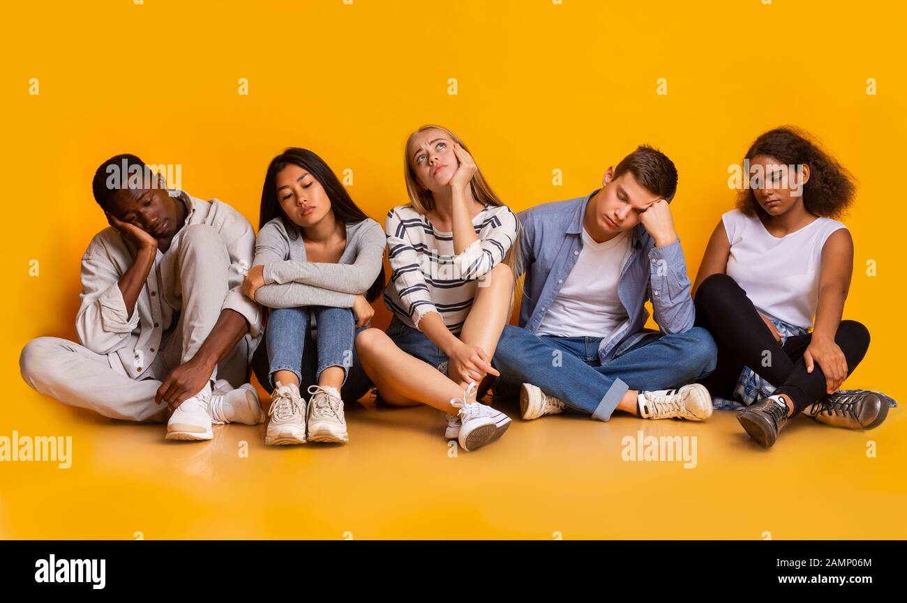 Bored classmates sitting over yellow background, being tired after ...
