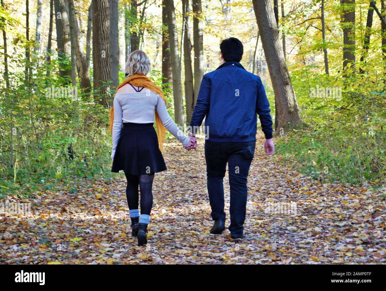 A young couple walking down a trail in the woods holding hands in the ...