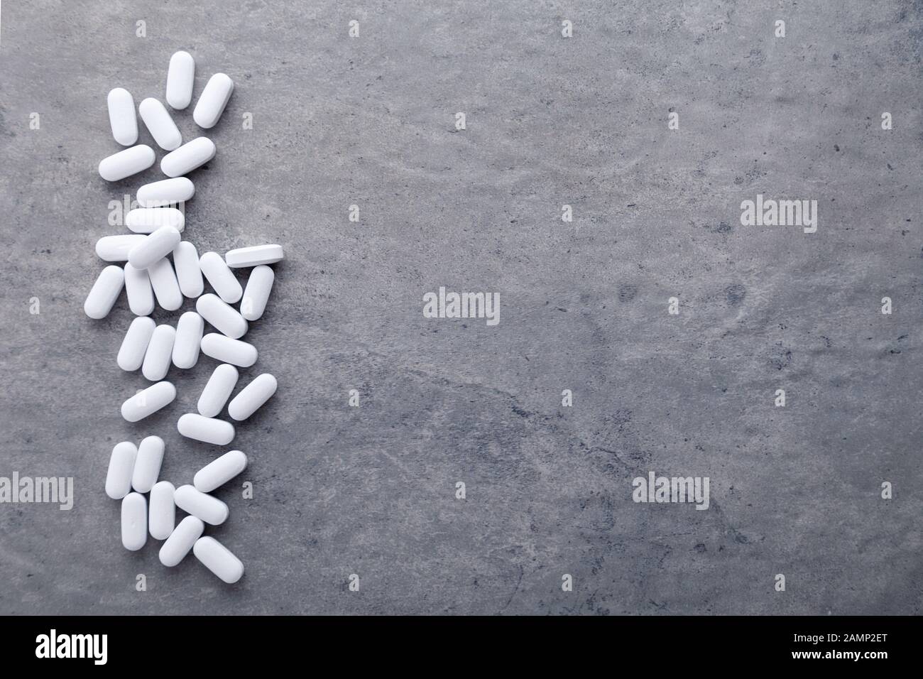 Closeup scattered white medicine vitamins, pills, drugs on gray ...