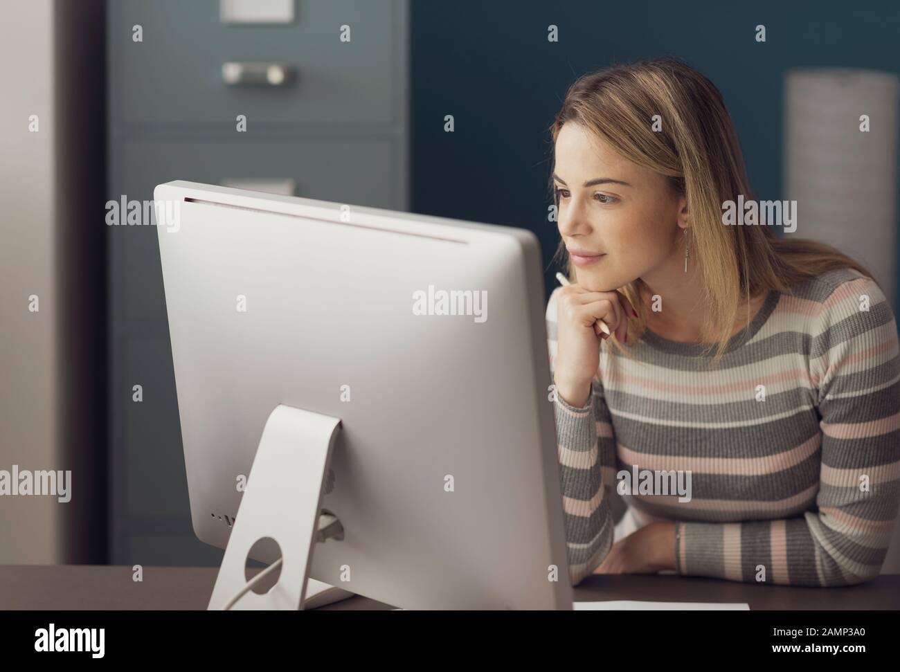 Young attractive woman sitting at desk and working with her computer ...