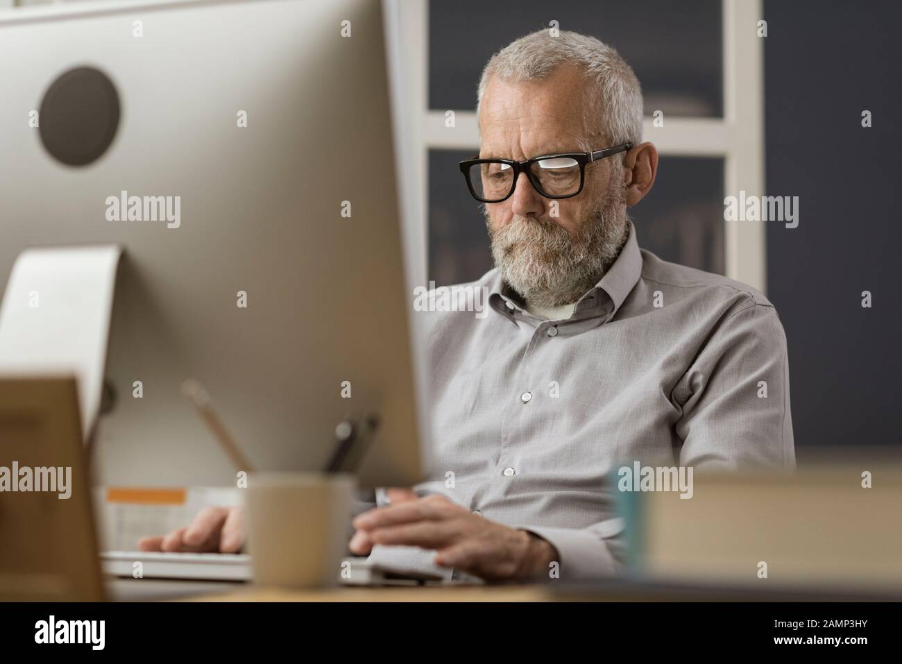 Senior retired man sitting at desk and working with a computer, elderly ...