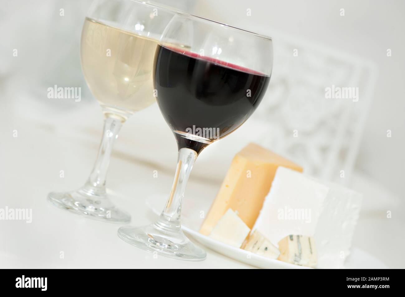 Glasses with red and white wine and cheese on a plate on a light ...