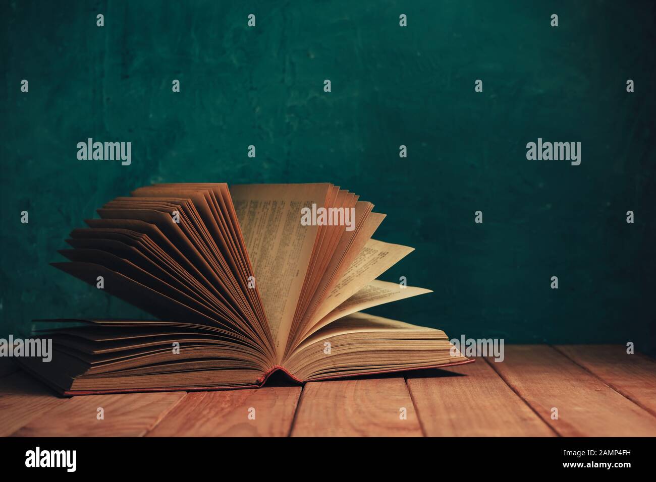 Close up beautiful open old book on a red wooden table. Green wall ...