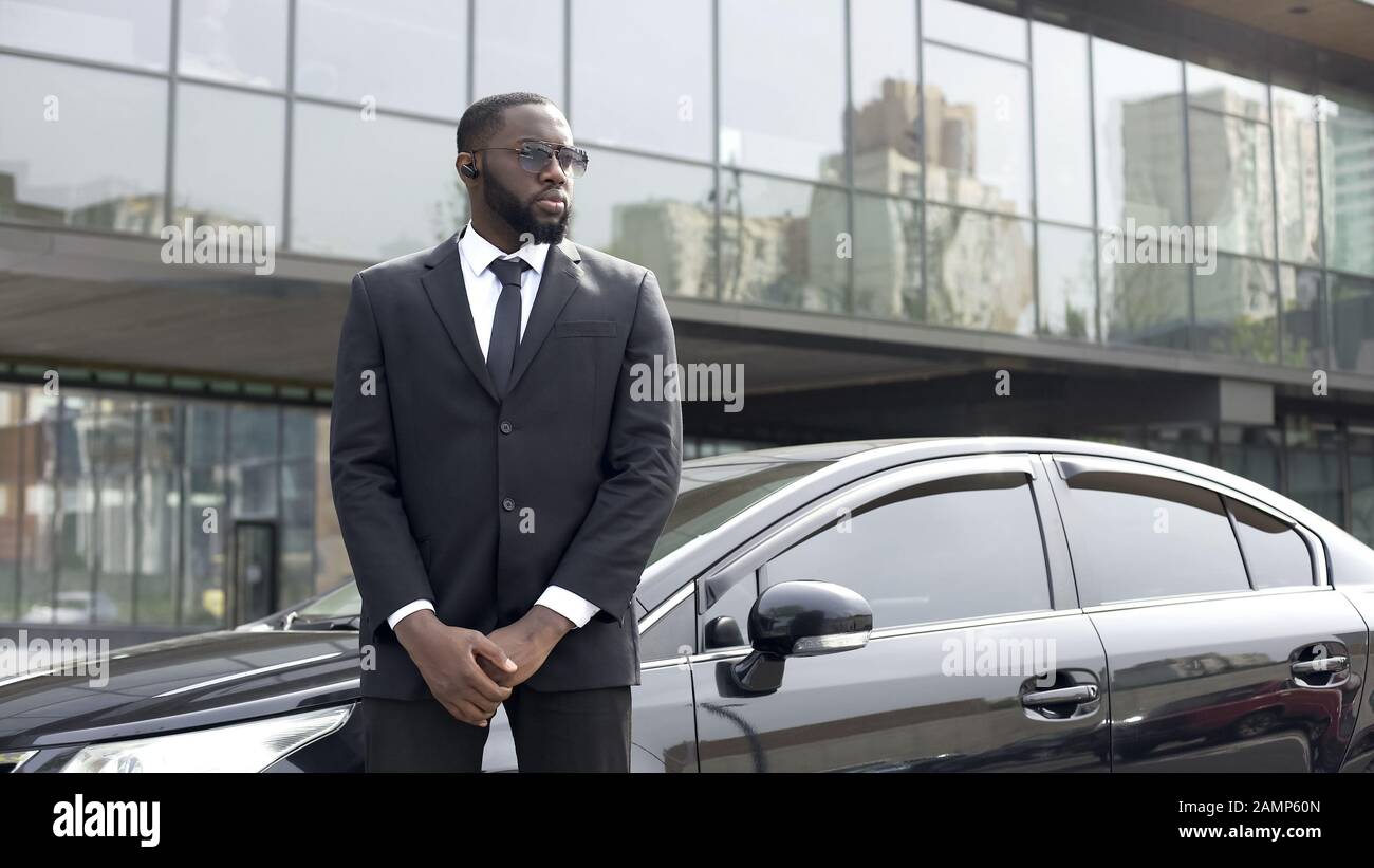 Confident Afro-American driver standing by car, security guard service ...
