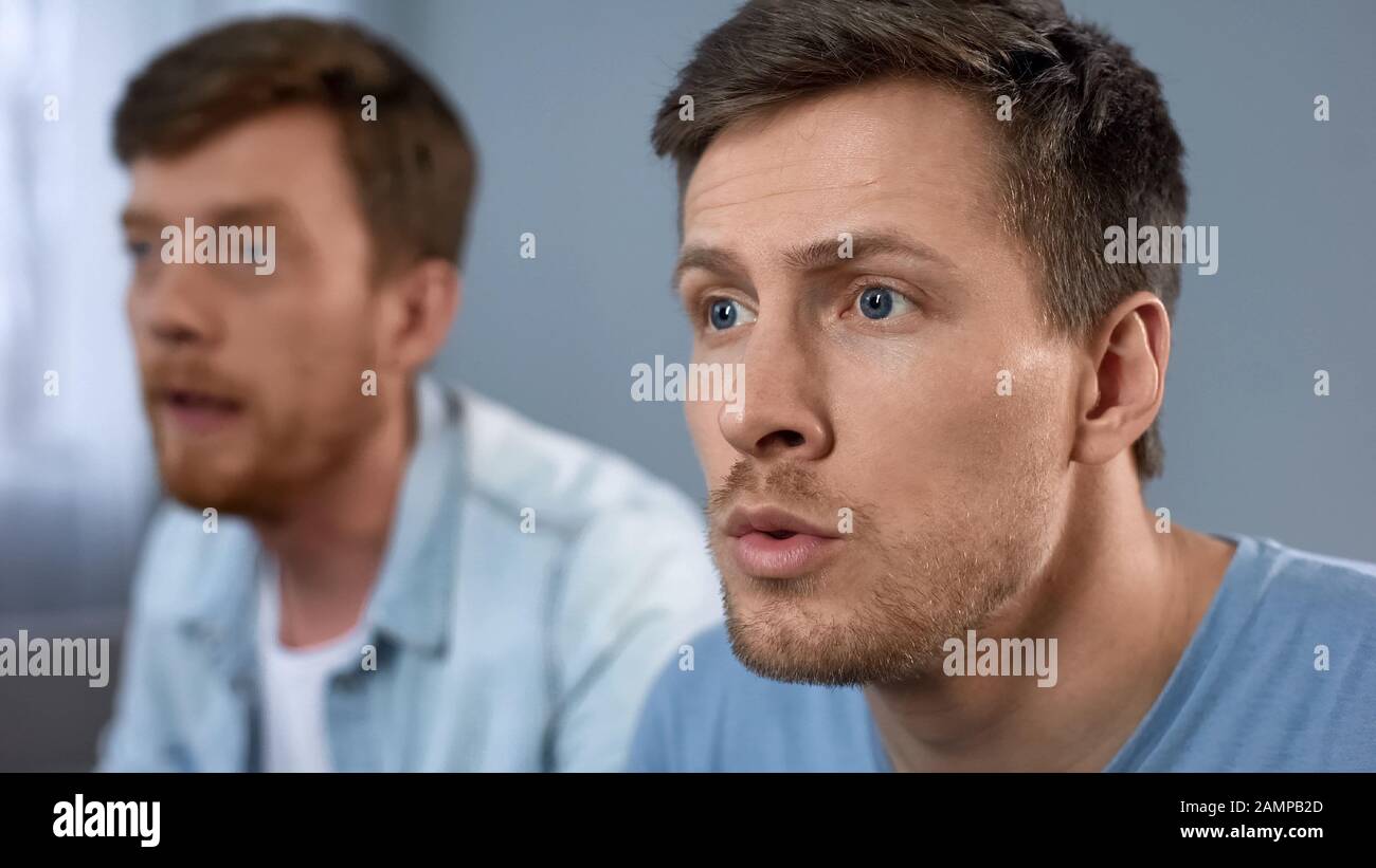 Two men watching sport game together on television at home, leisure ...