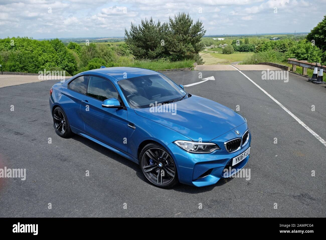 BMW M2 standing on a road with trees in the middle distance and clouds ...